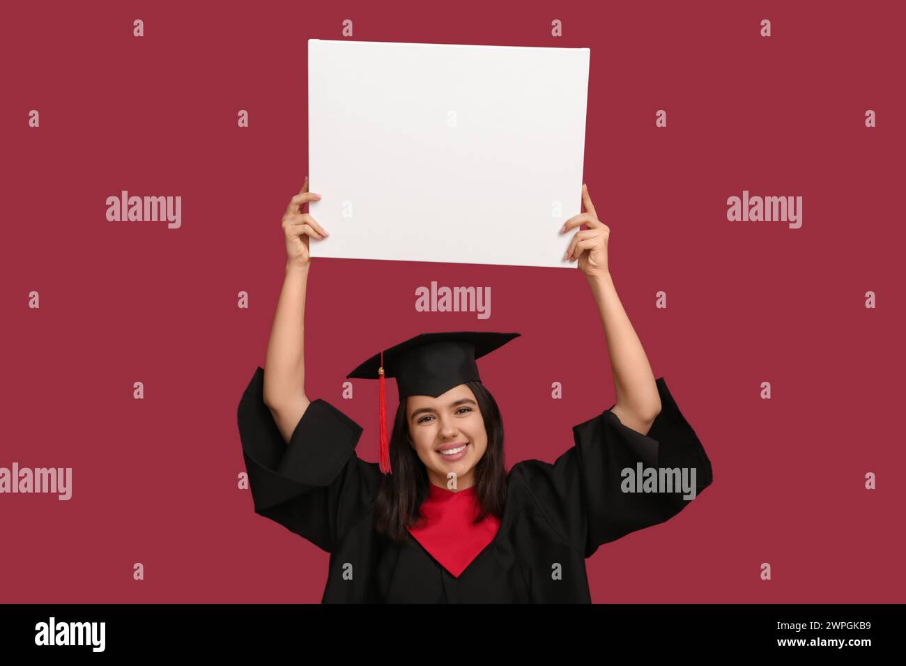 Happy female graduating student with blank poster on red background ...