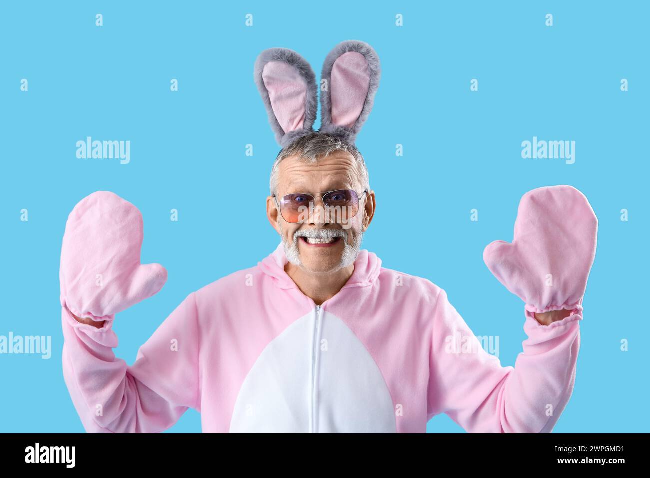 Funny senior man in Easter bunny costume and sunglasses on blue ...