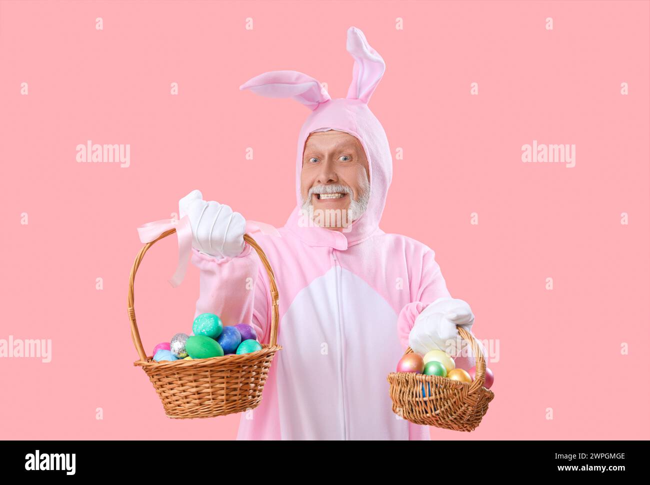 Senior man in bunny costume holding wicker baskets with Easter eggs on ...