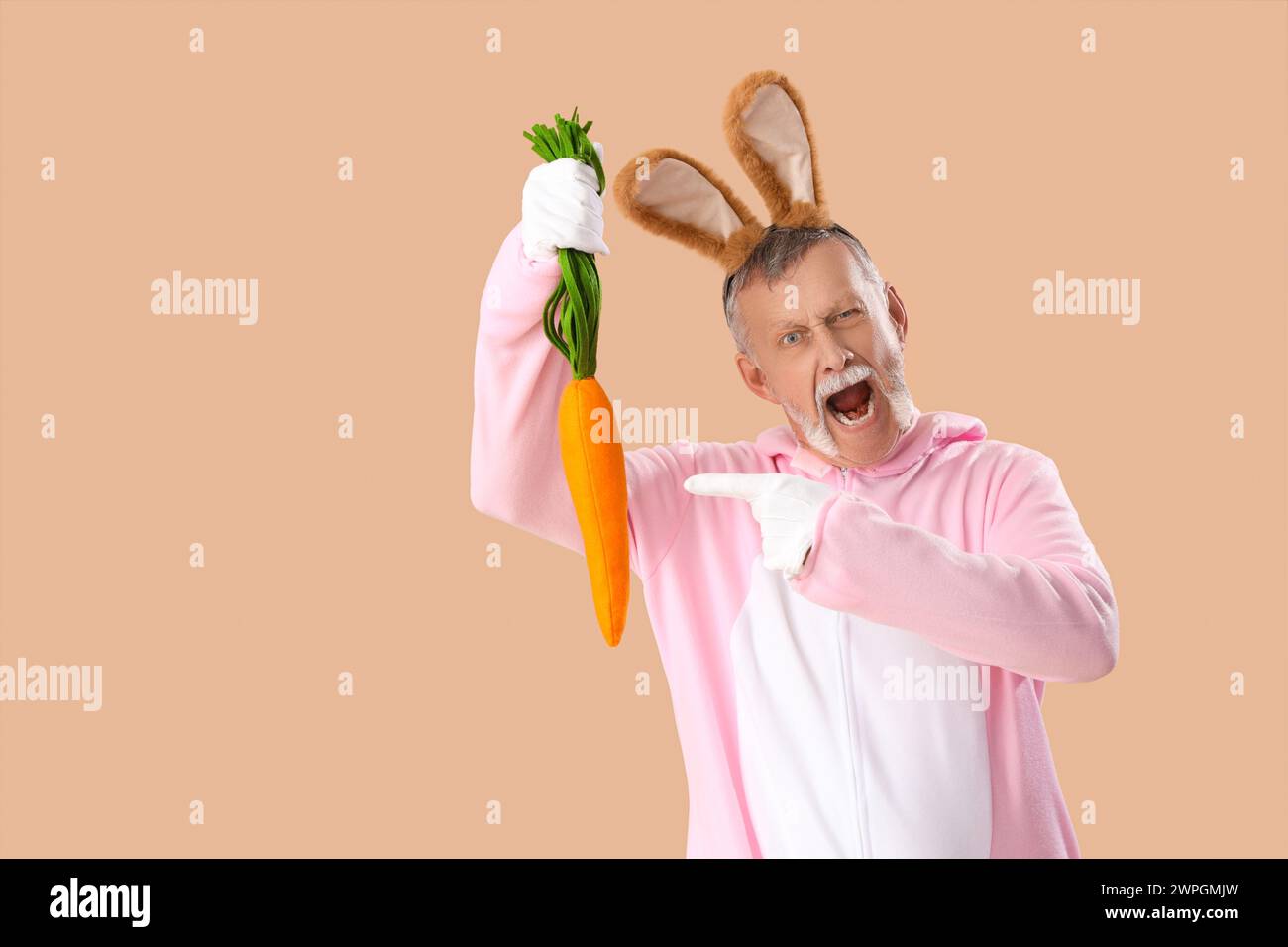 Senior man in Easter bunny costume with plush carrot on beige ...