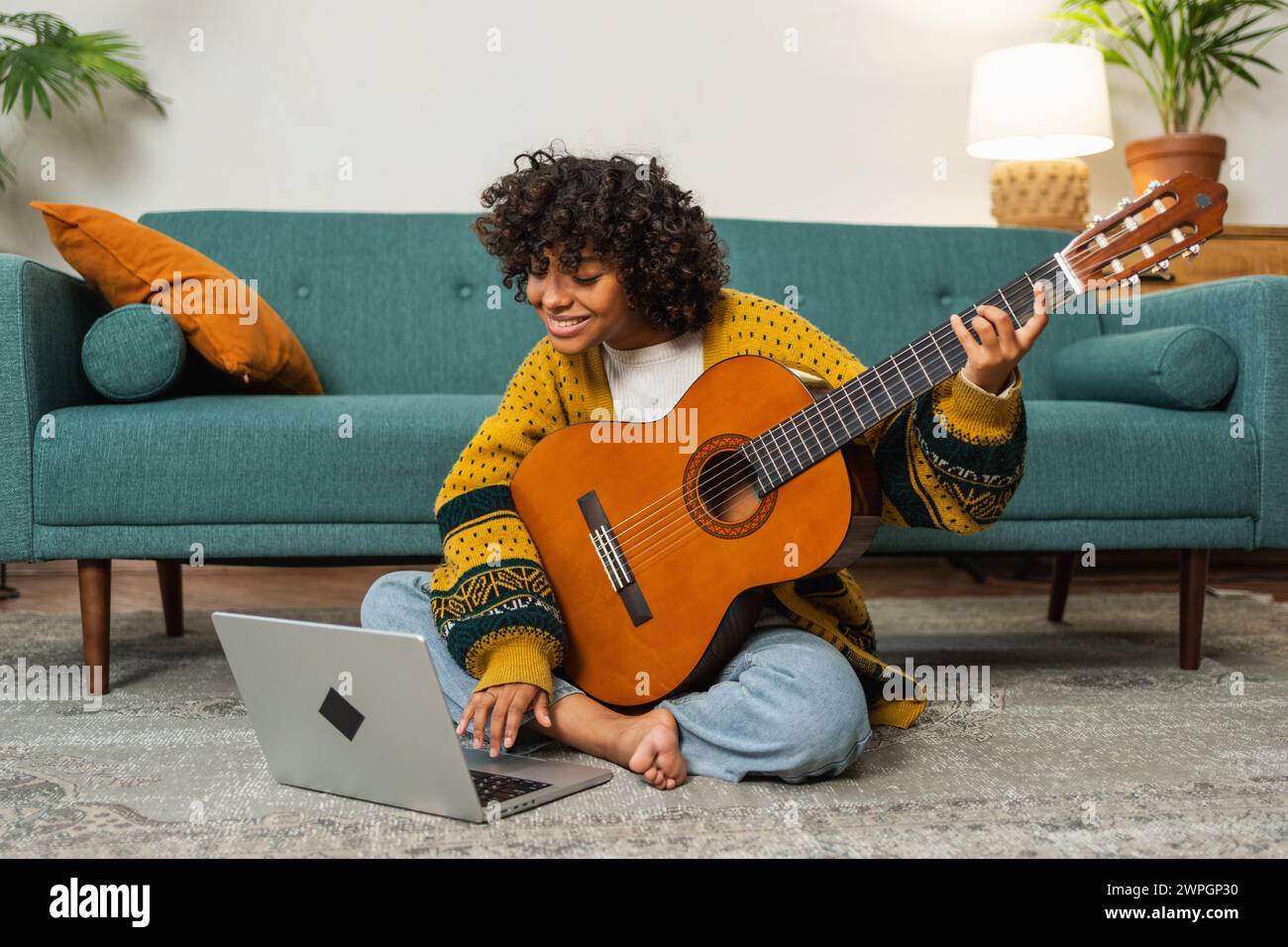 African American woman learning guitar watching tutorial on laptop at ...