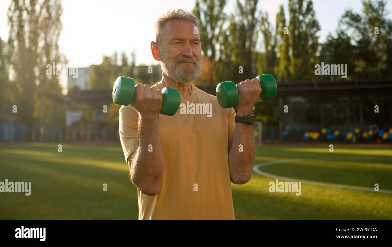 Old Caucasian man grandfather lift dumbbell pump biceps sport athlete ...