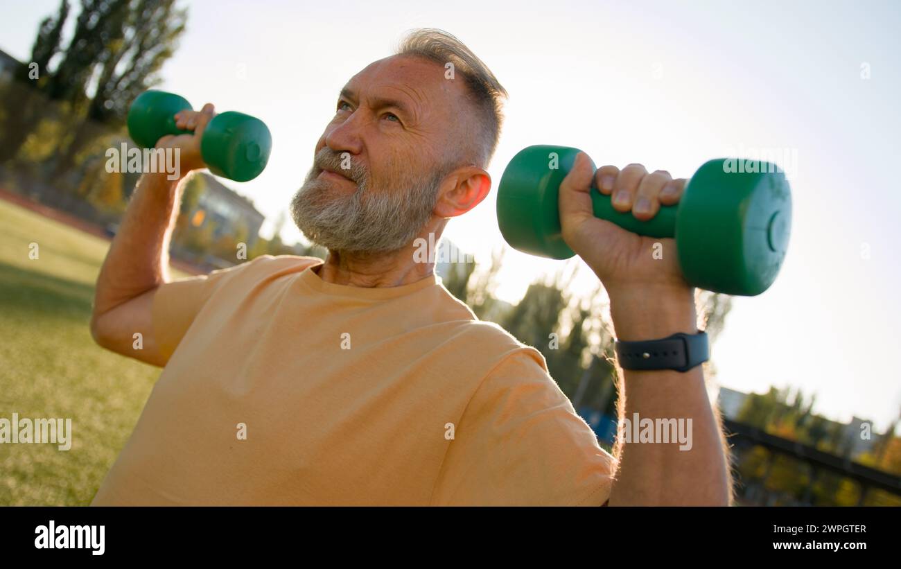 Aged Caucasian European man sportsman lifting dumbbell weightlifting energy training bodycare ...