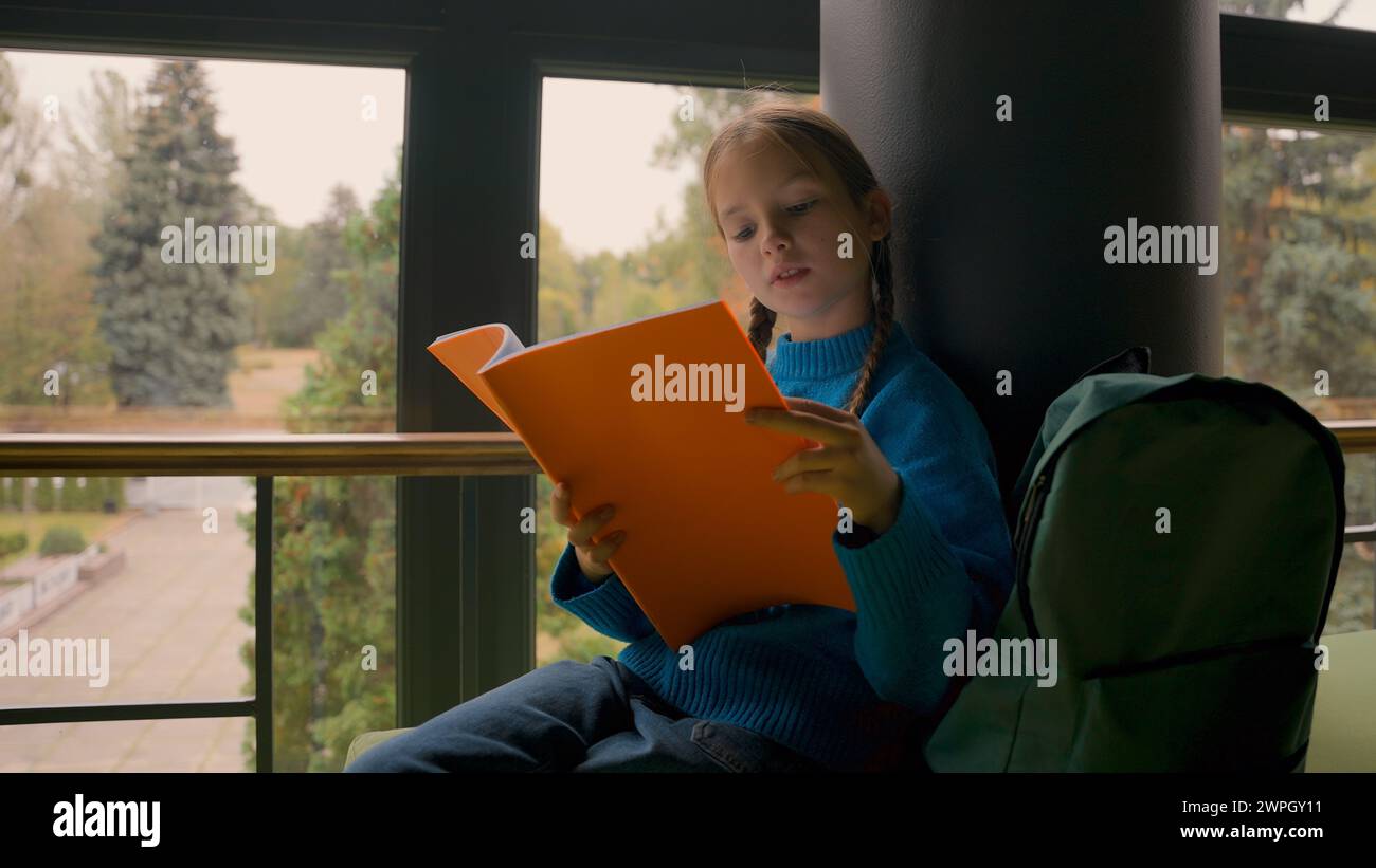 Little girl sitting school hall reading textbook prepare exam task ...