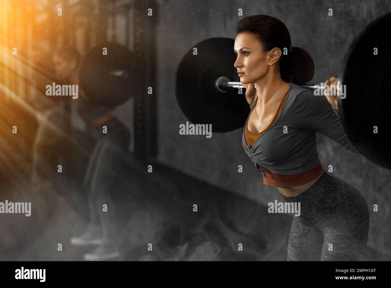 Slender woman trains muscles of arms and back using barbell and ...