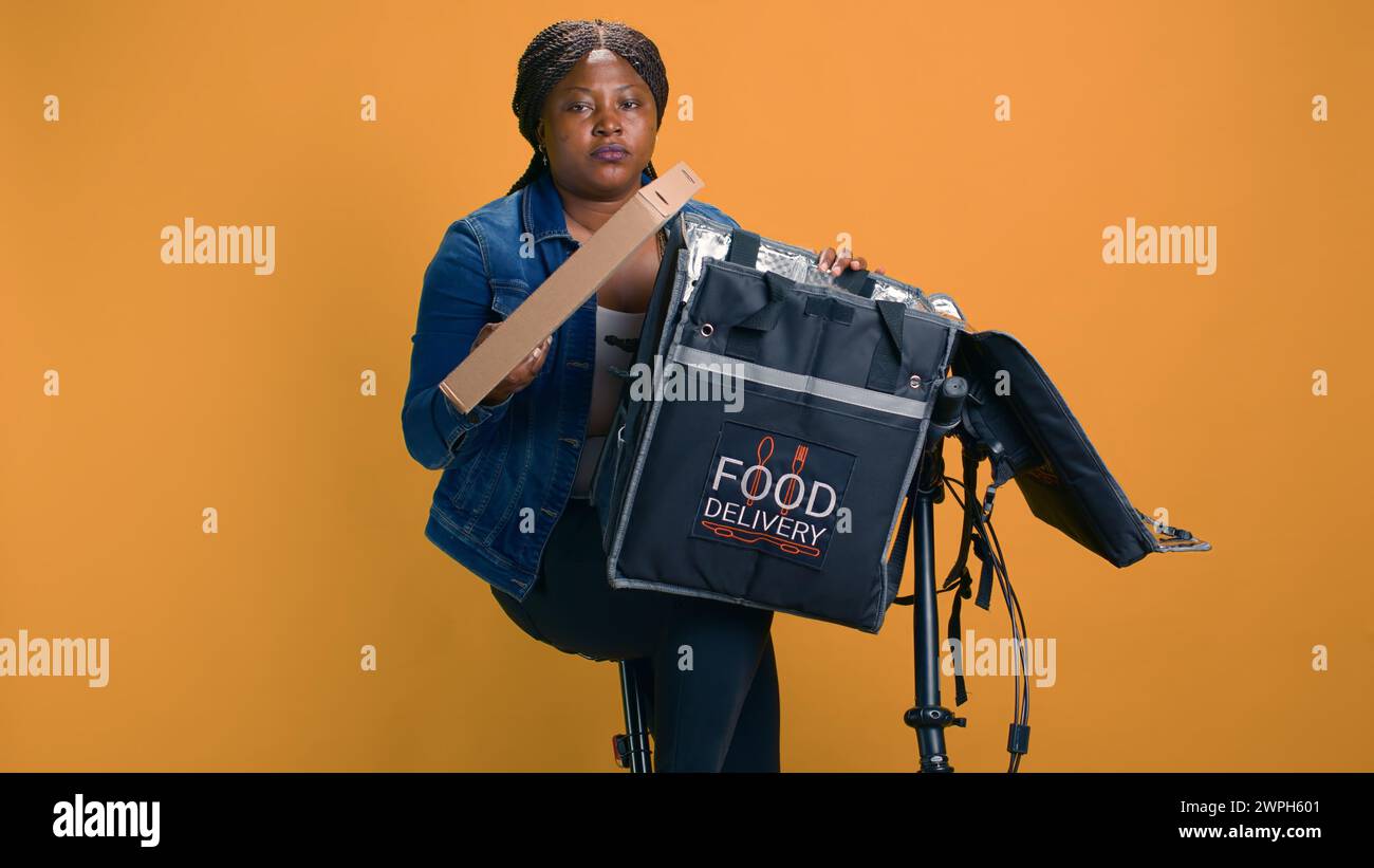 Black woman on bicycle carefully delivering fresh takeout meal with ...