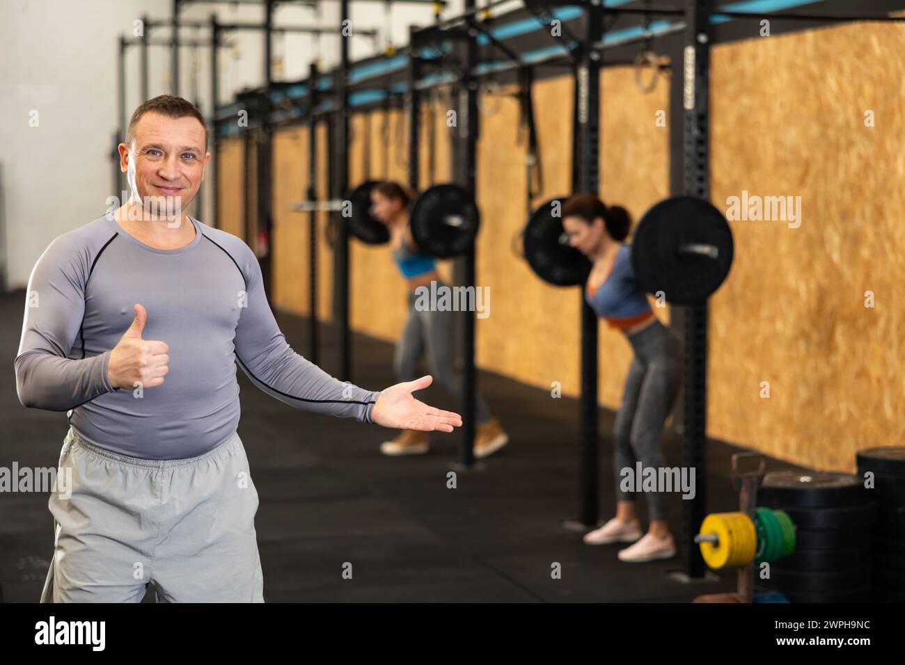 Positive middle-aged trainer with thumbs-up gesture in gym Stock Photo ...