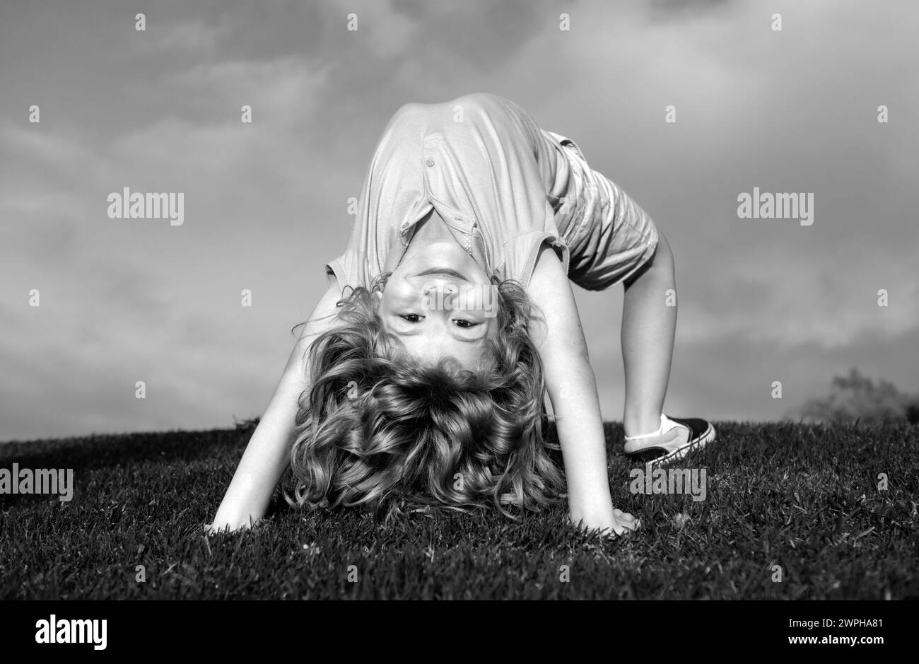 Happy child standing upside down on green grass. Laughing kid boy ...