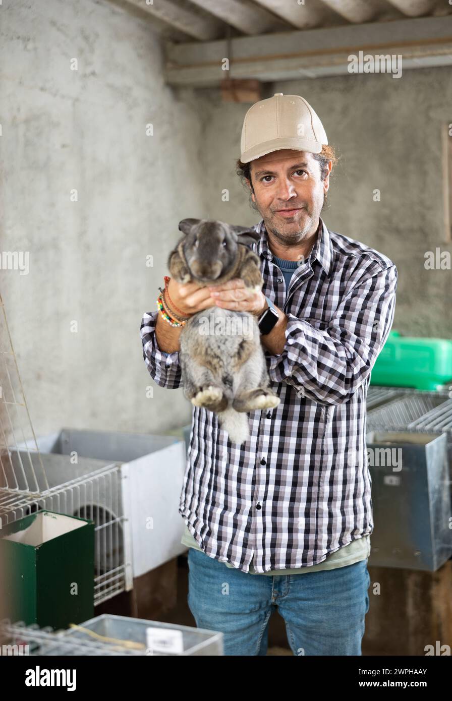 Man farmer with rabbit in her hands on her farm. Farmer takes care of ...