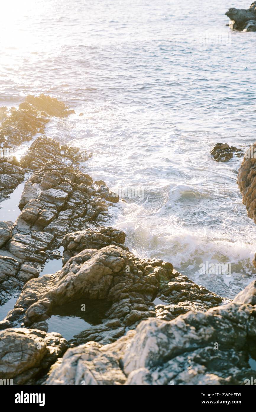 Sea surf rolls over the rocks in the sun rays Stock Photo - Alamy