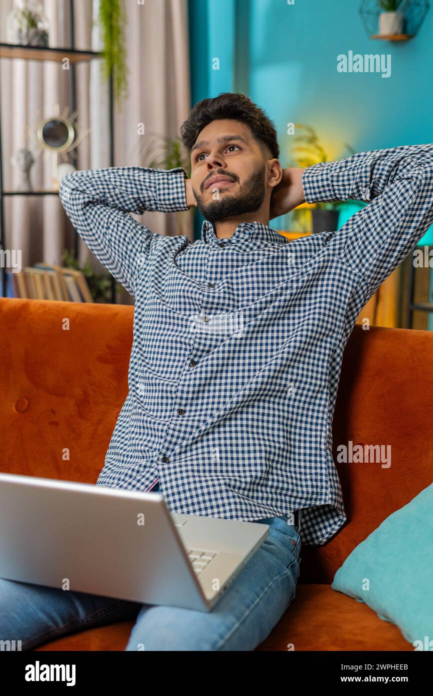 Indian man sitting on couch closing laptop after finishing work in ...