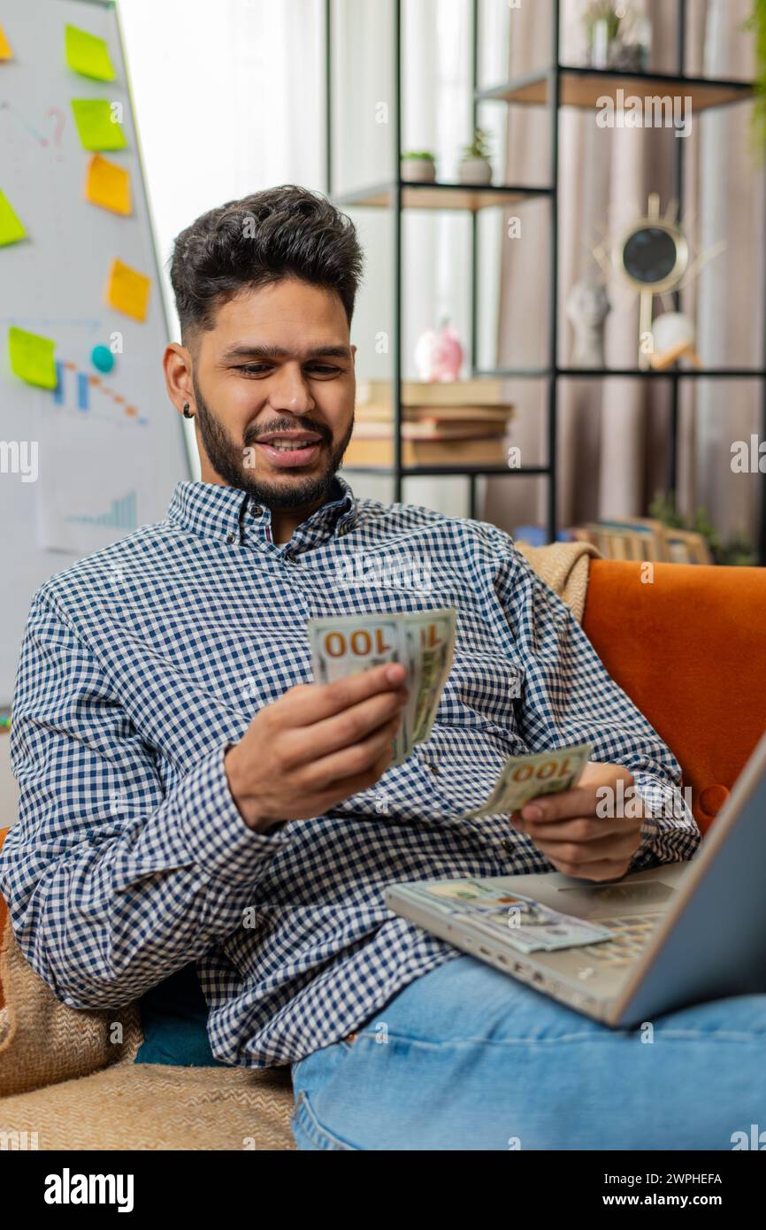 Planning budget. Rich happy Indian man counting money cash use laptop ...