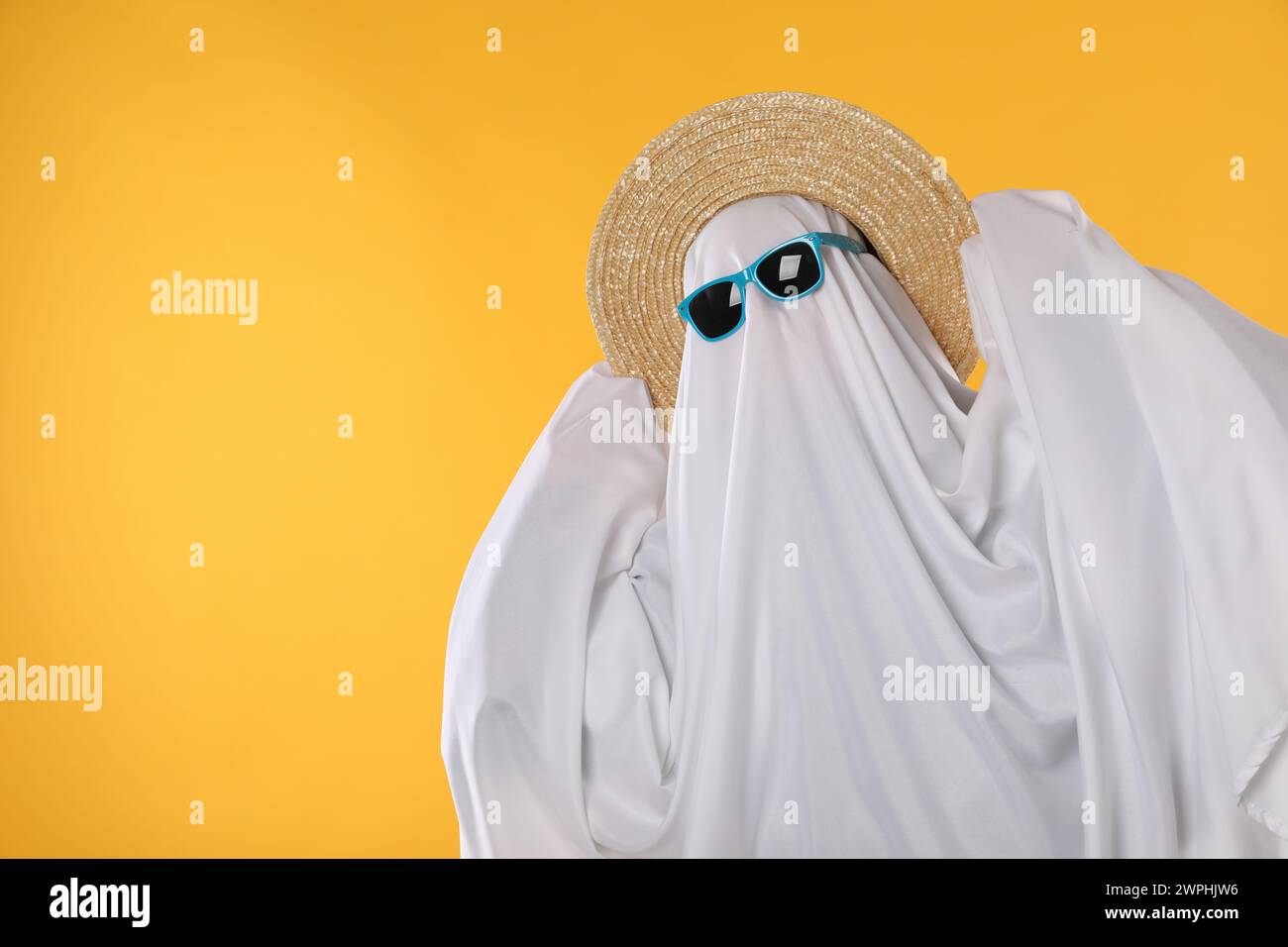 Person in ghost costume, sunglasses and straw hat on yellow background ...