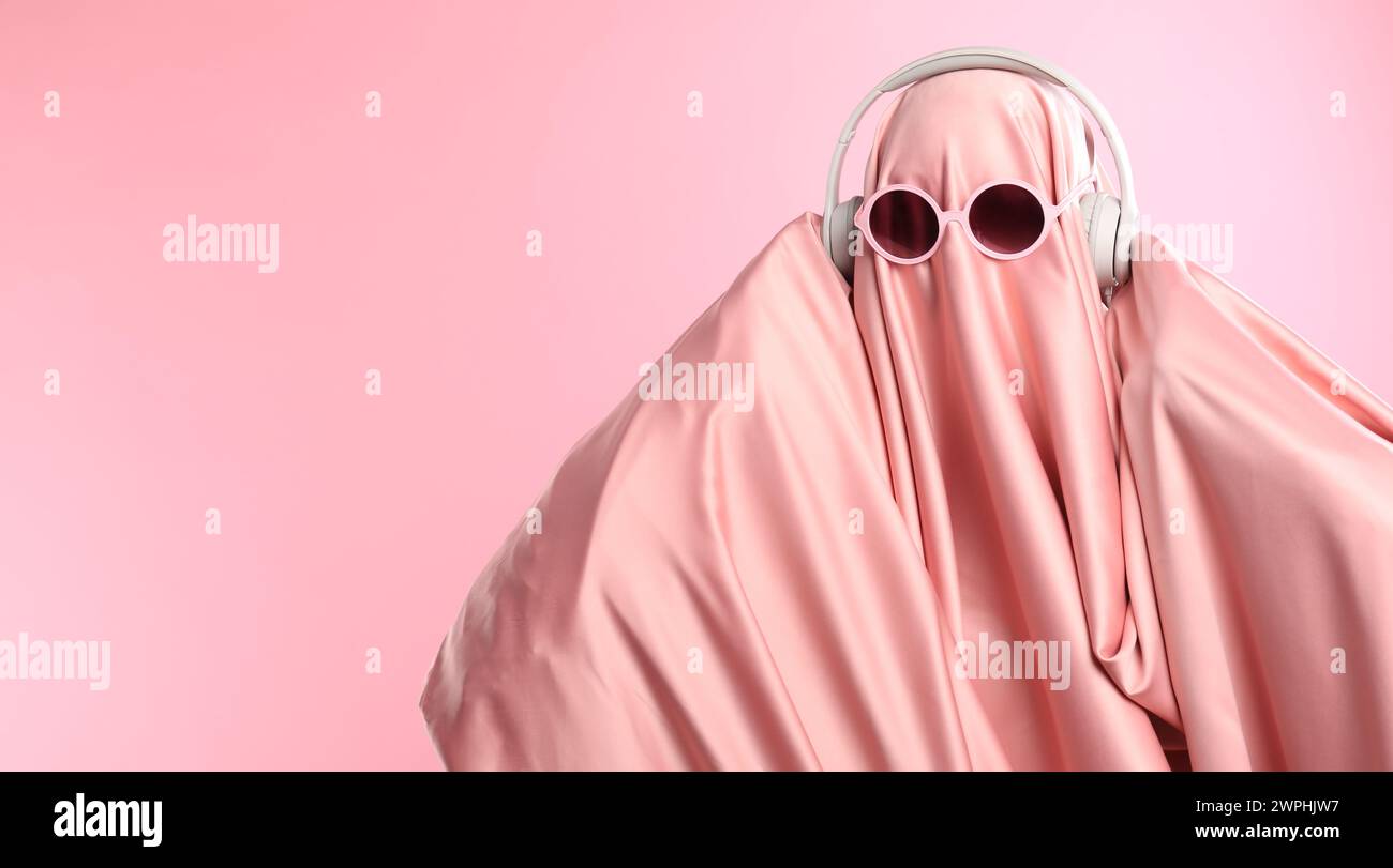 Glamorous ghost. Woman in sheet with sunglasses and headphones on pink ...