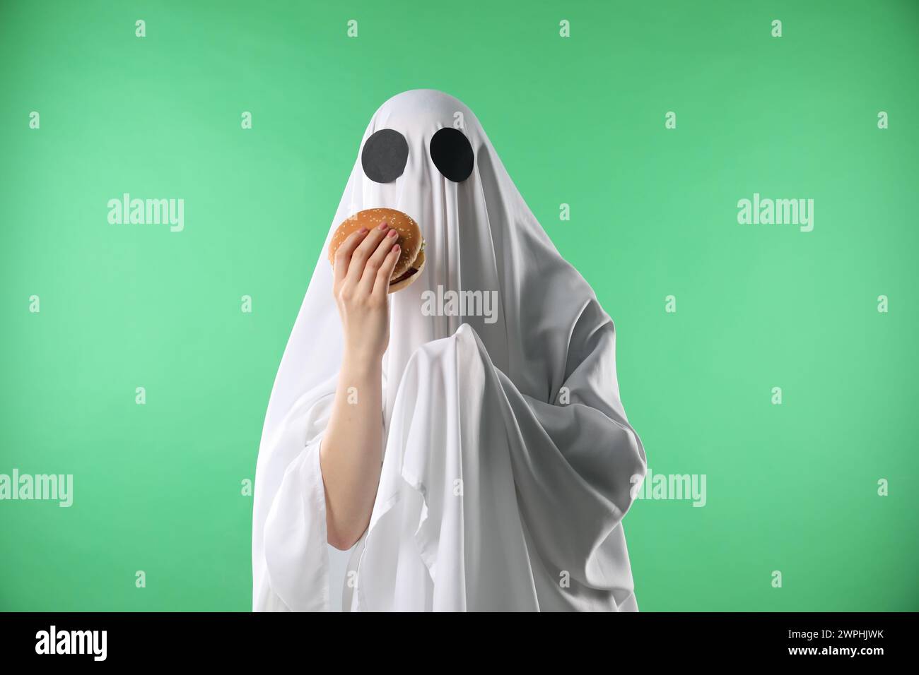 Creepy ghost. Person in white sheet with tasty hamburger on green ...