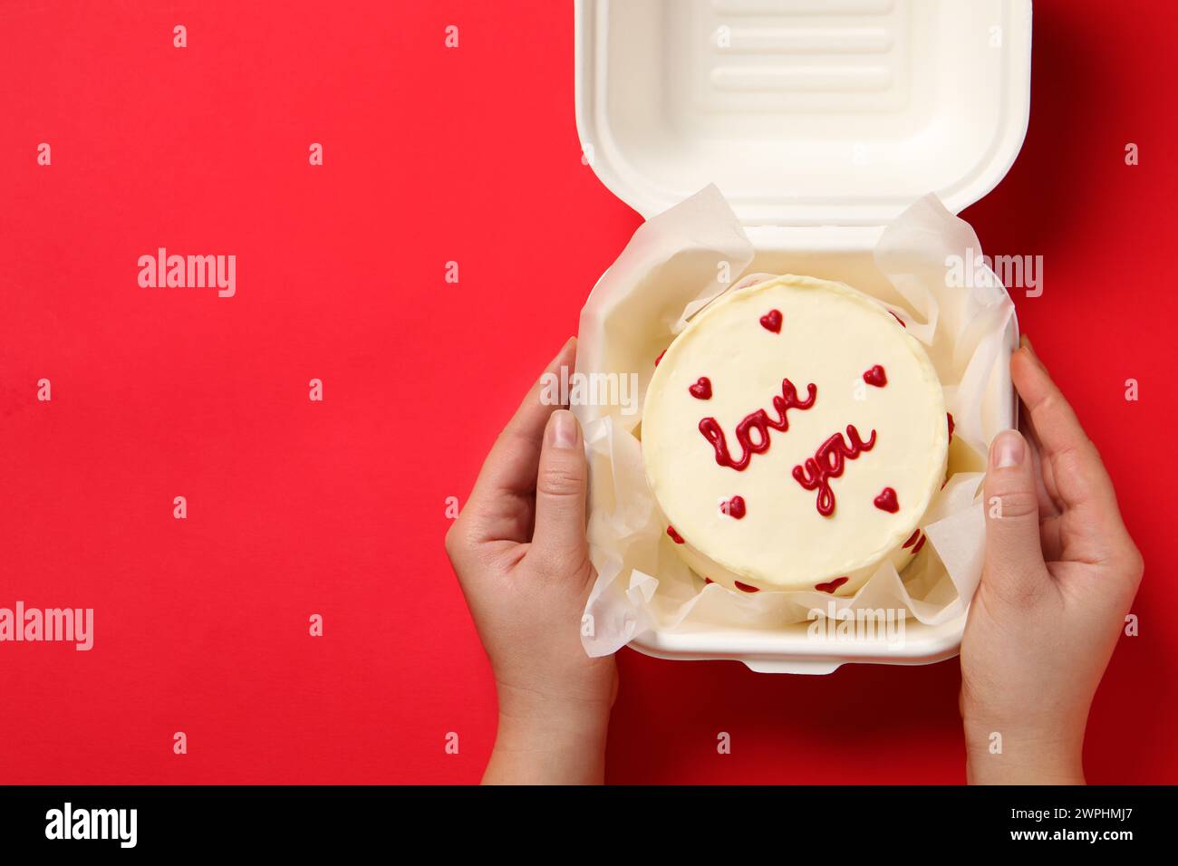 Woman holding takeaway box with bento cake at red table, closeup. St ...