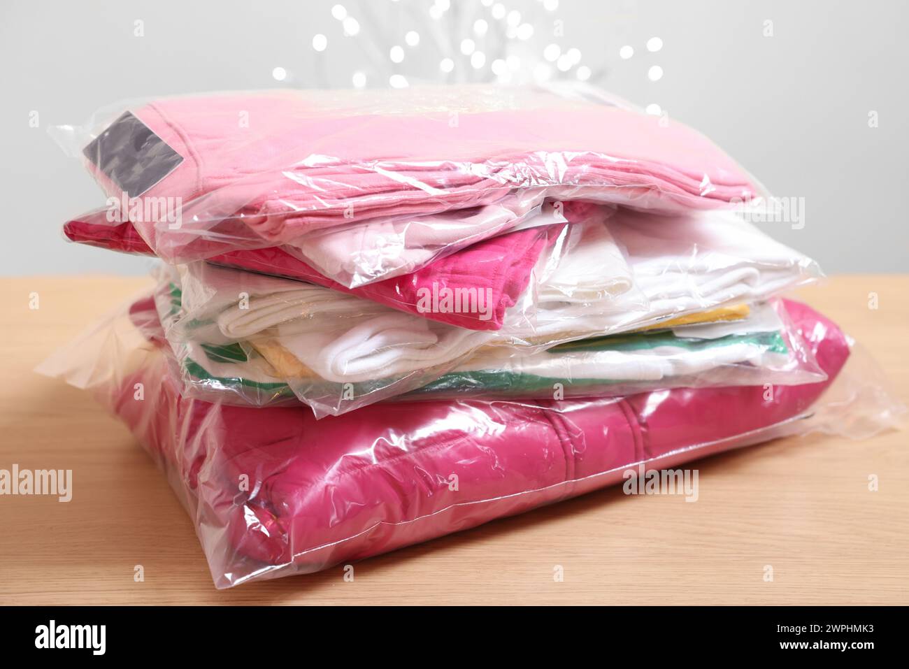 Stack of folded clothes in plastic bags on wooden table against beige ...