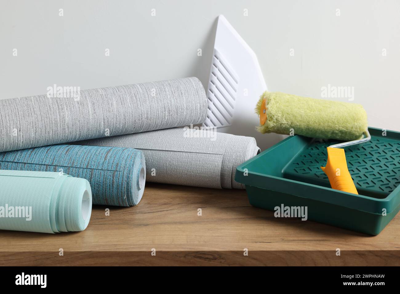 Different wallpaper rolls, roller and plastic spatula on wooden table ...