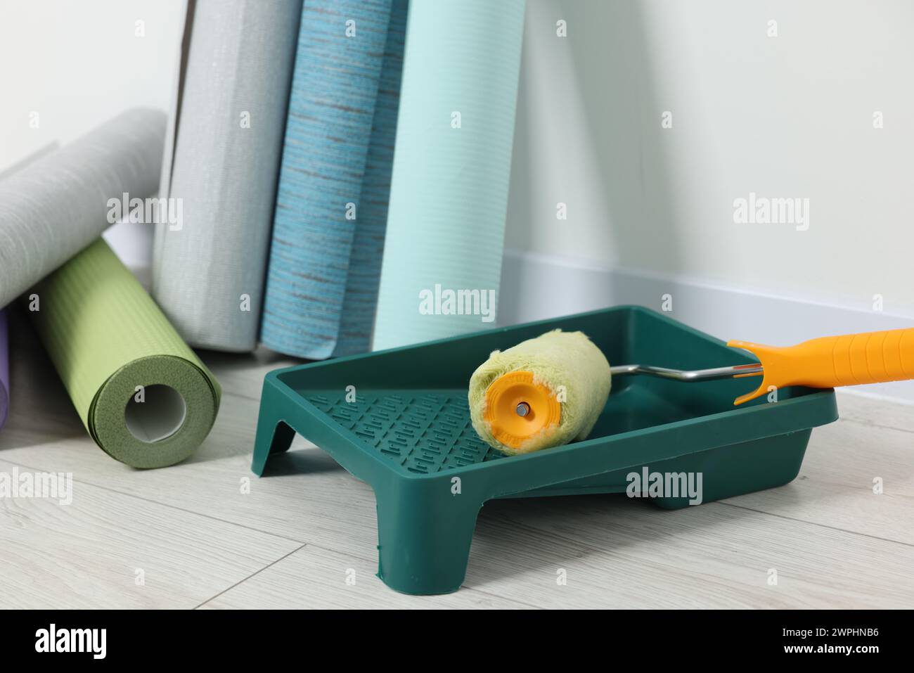 Different wallpaper rolls, roller and tray near white wall indoors ...