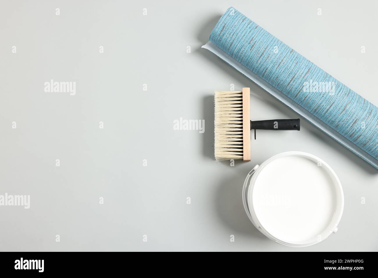 Blue wallpaper roll, brush and bucket with glue on light background ...