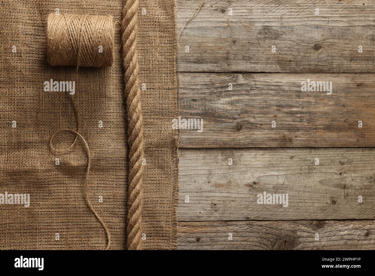 Burlap fabric, spool of thread and jute on wooden table, top view ...