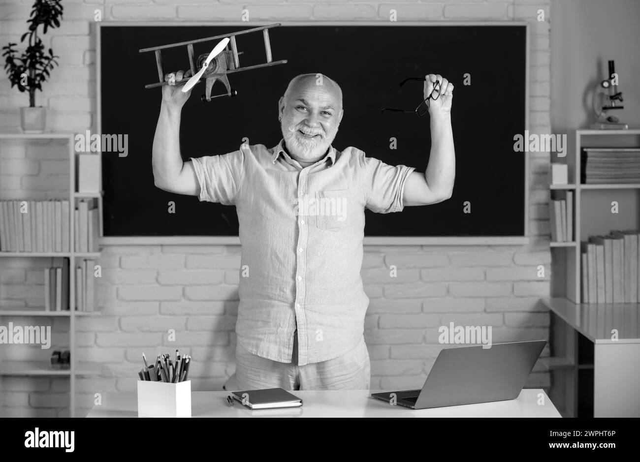 Funny senior teacher in the classroom on blackboard background. Old fun ...