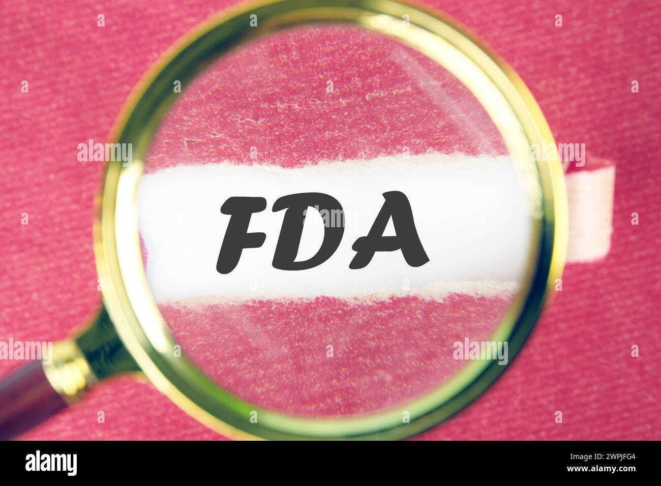Word FDA through a magnifying glass under a torn piece of red paper ...