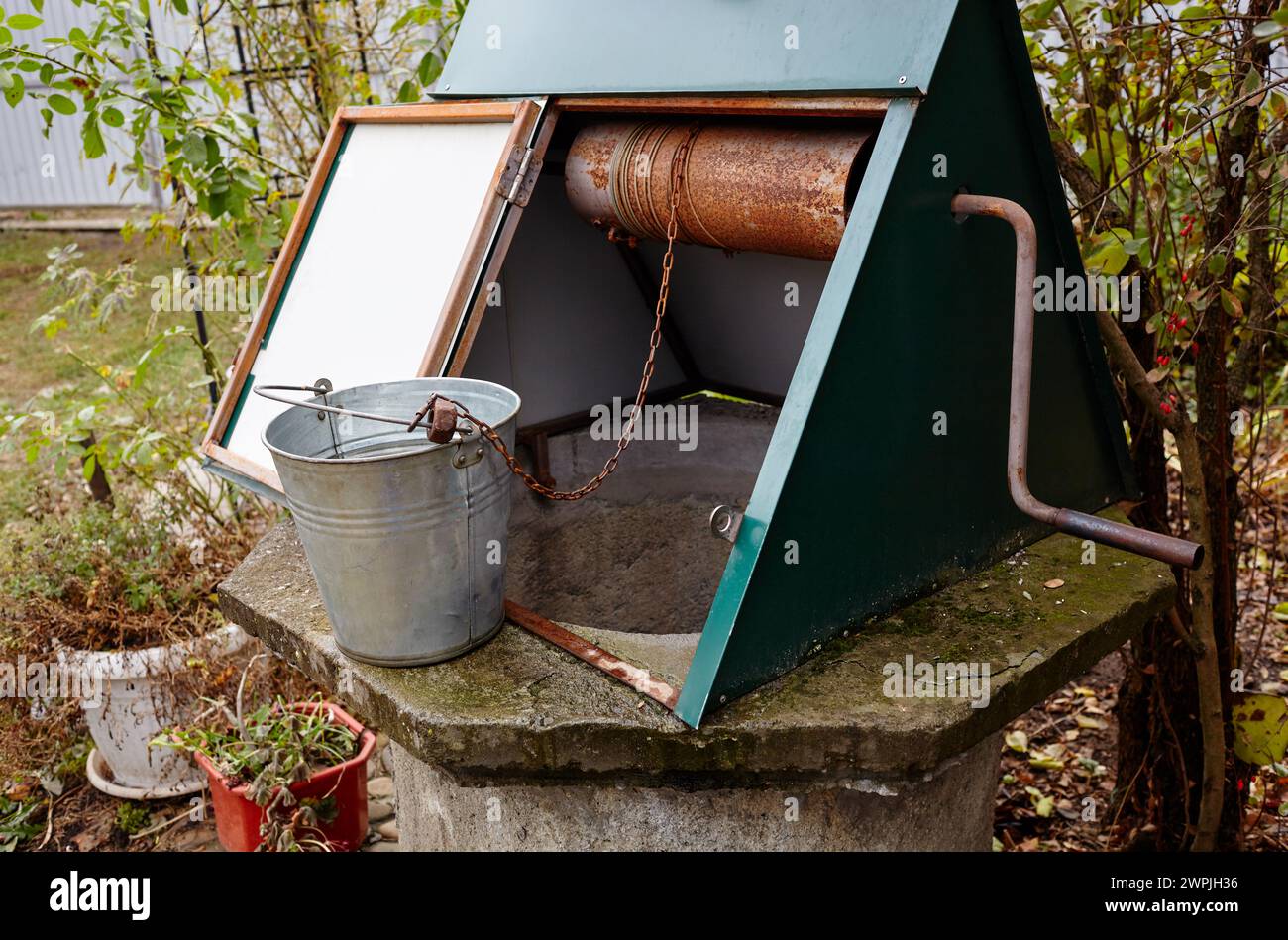 Metal bucket at draw-well in European village. Retro stone water well ...