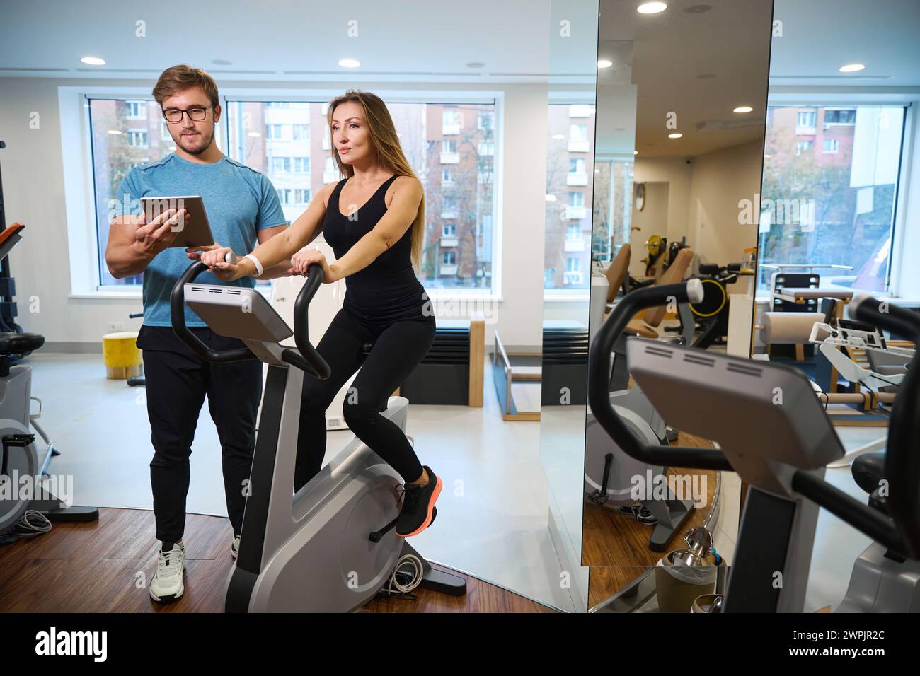 Instructor in a gym monitors a clients workout on an exercise bike Stock Photo - Alamy