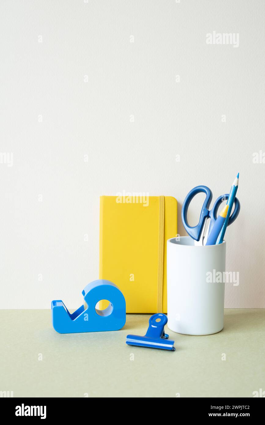 Yellow notebook, blue colored pencil, pen, scissors, clip, tape ...