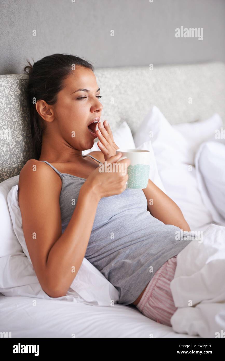 Woman, bedroom and coffee in morning with yawn for waking up, tired and ...