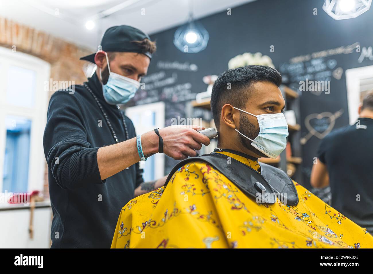Professional barber wearing mask trimming neck hair of his client in ...