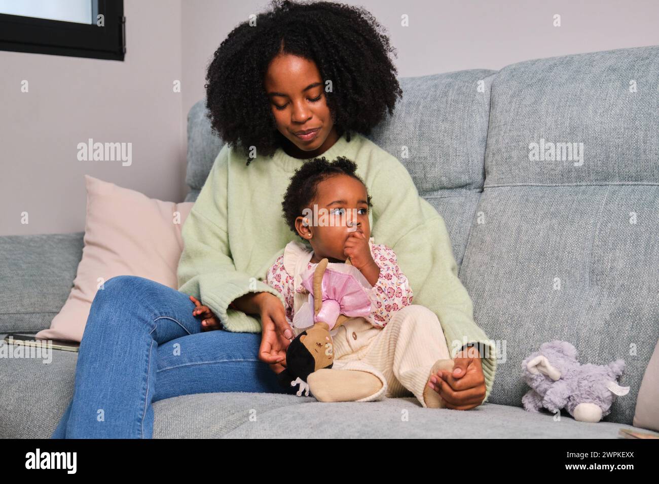 Cuban mother with her toddler daughter sitting on the sofa at home ...