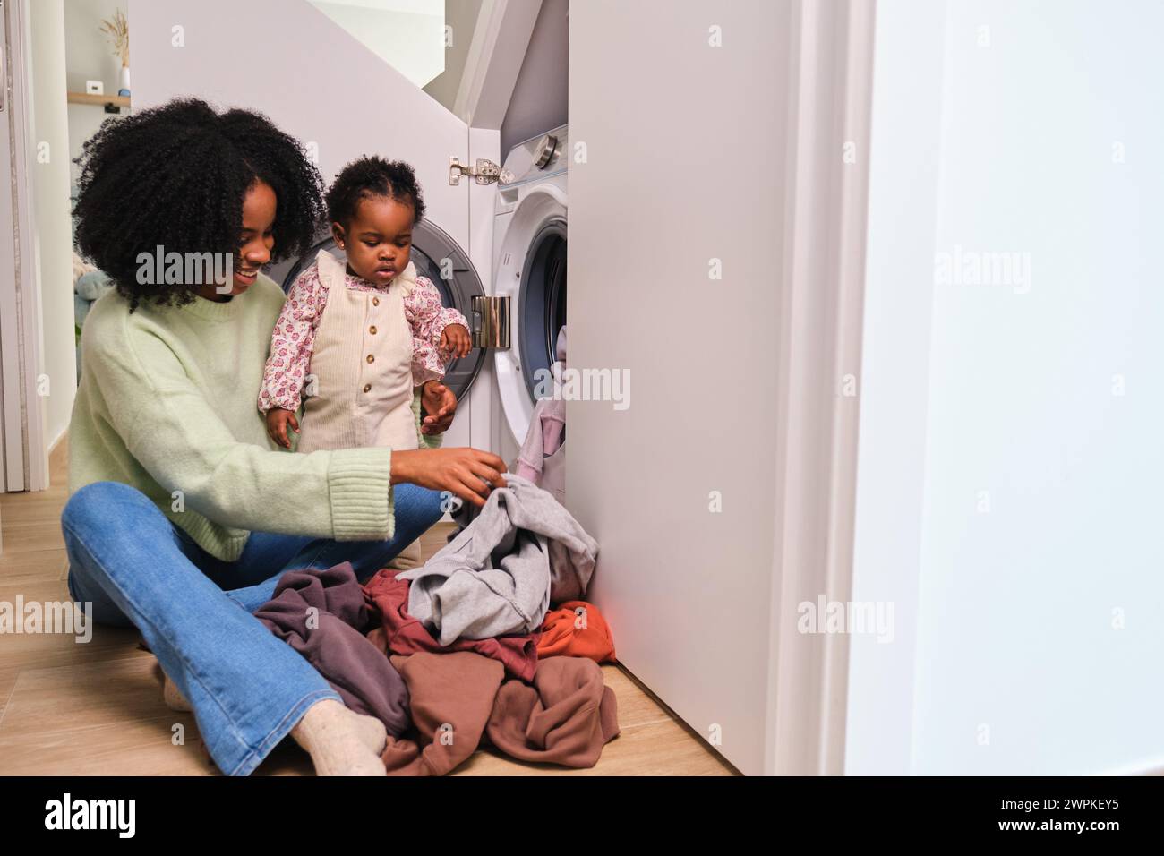Cuban mother placing clothes in washing machine with her daughter Stock ...