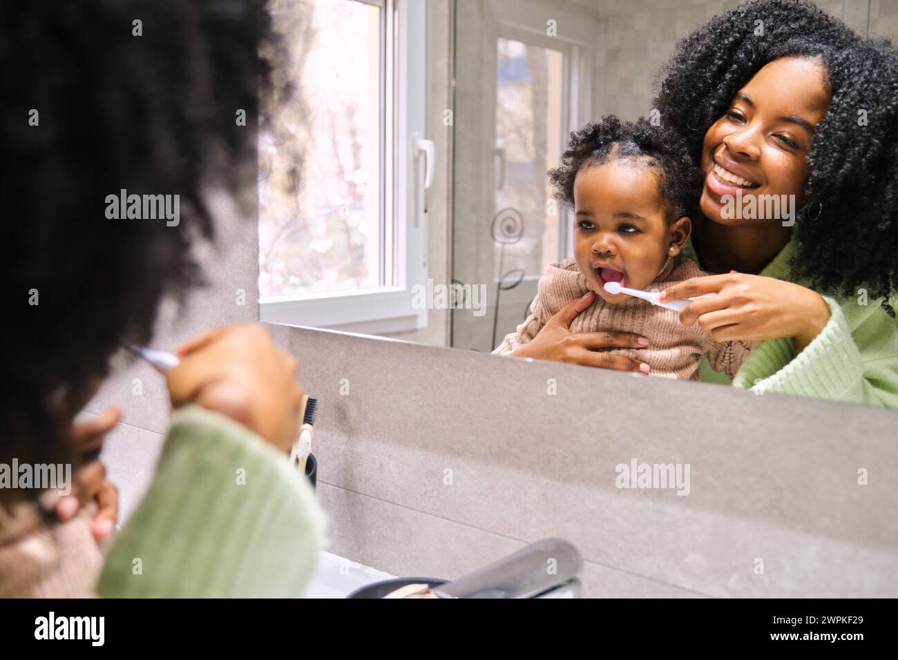 Cuban mother brushing her toddler daughter's teeth in the bathroom ...