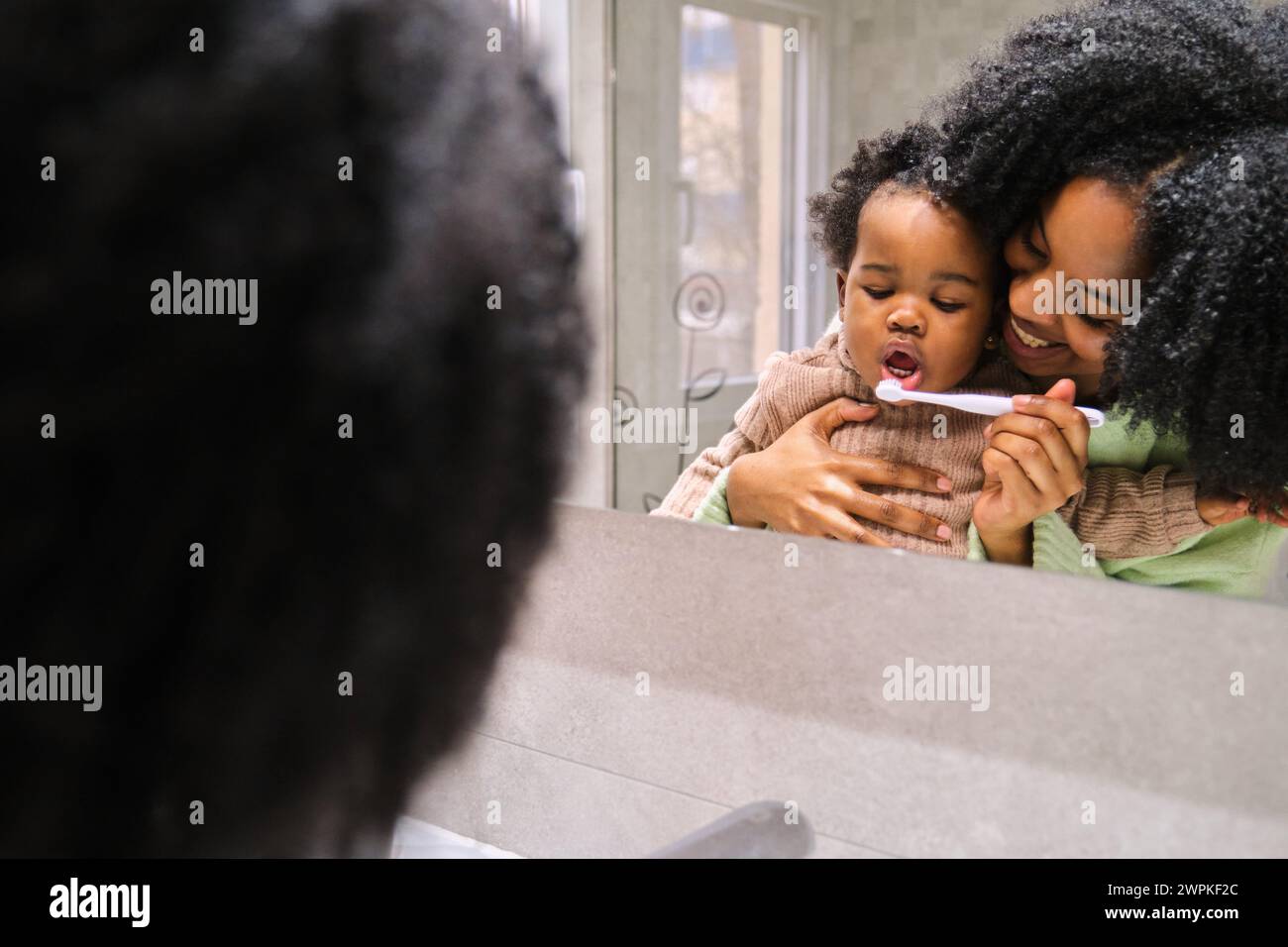 Cuban mother brushing her toddler daughter's teeth with toothbrush ...