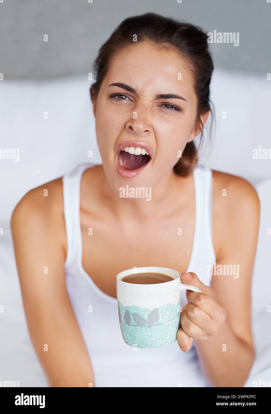 Woman, tired and yawning with coffee in bed, waking up from sleeping or ...