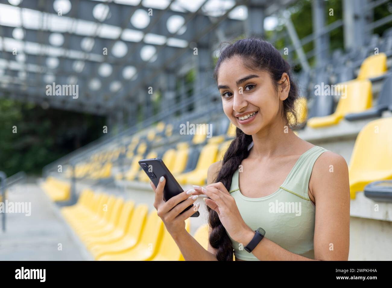 Cheerful young Indian woman syncing fitness smartwatch with phone at ...