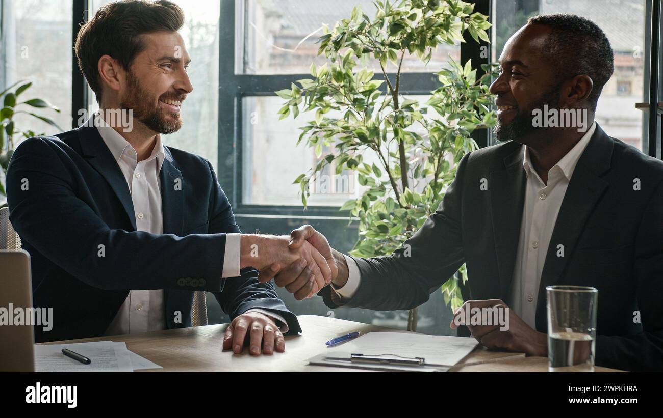 Two diverse multiracial businessmen signing document agreement shaking ...
