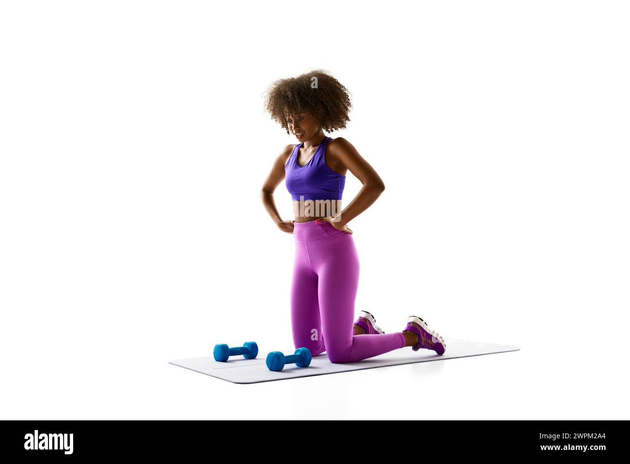 Woman in purple activewear kneeling on mat beside blue dumbbells ...