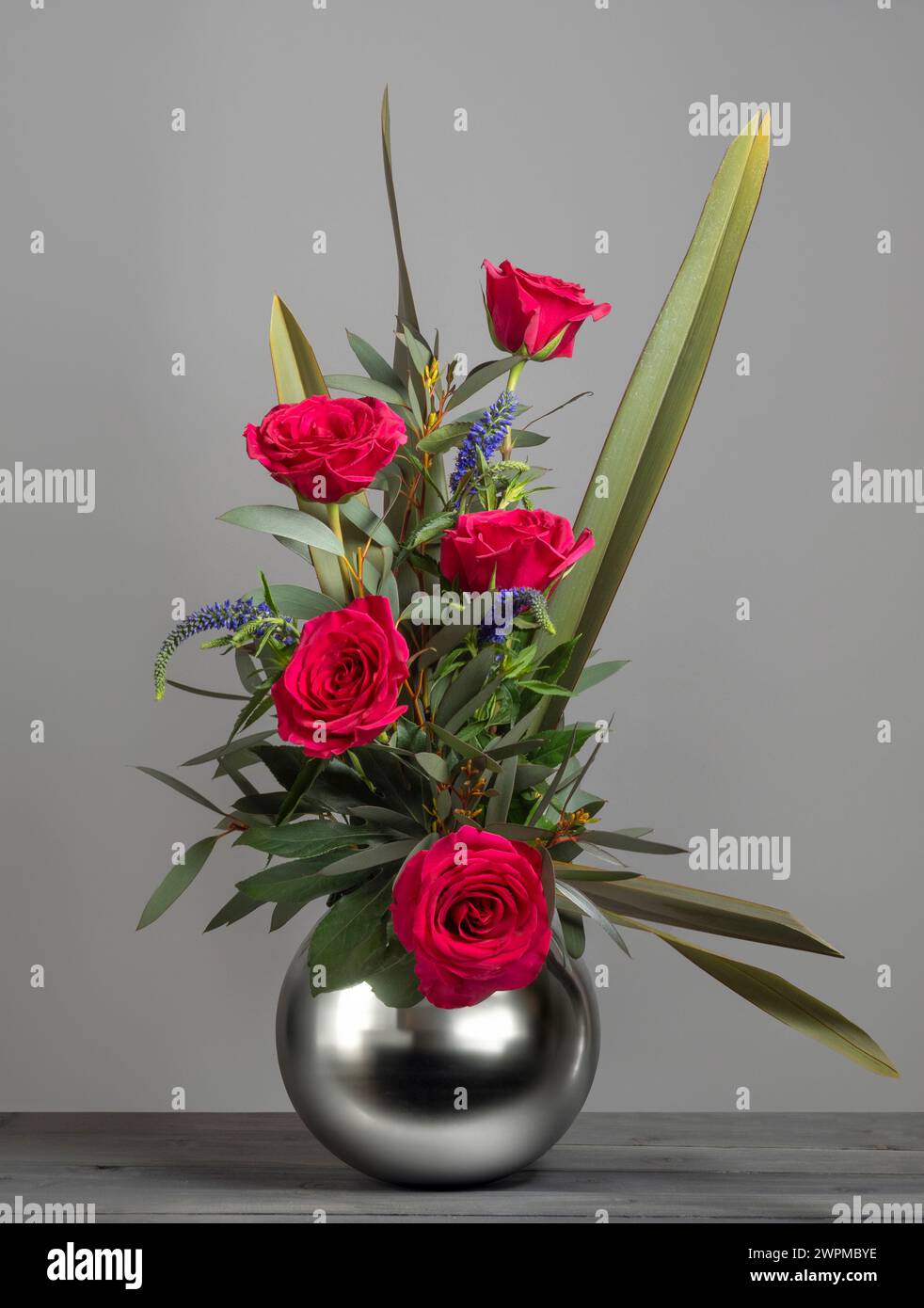 Red roses arranged in a spherical mirrored vase, seen against a grey ...
