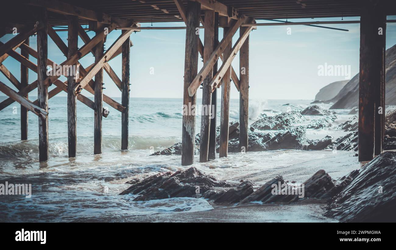 An ocean view with pier posts, water, and rocks below Stock Photo - Alamy