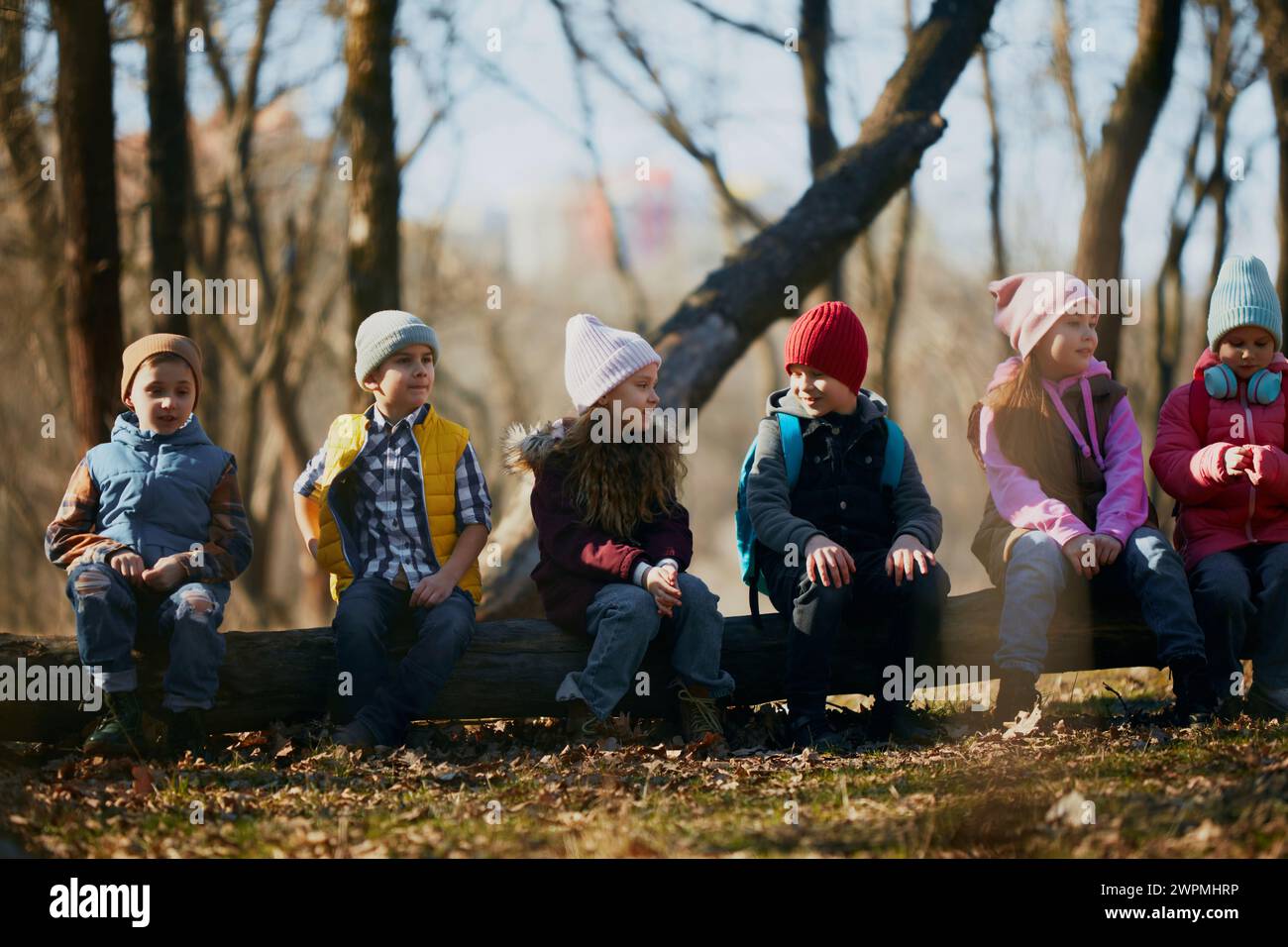Row of kids, classmates perched on a log, clad in colorful winter wear ...