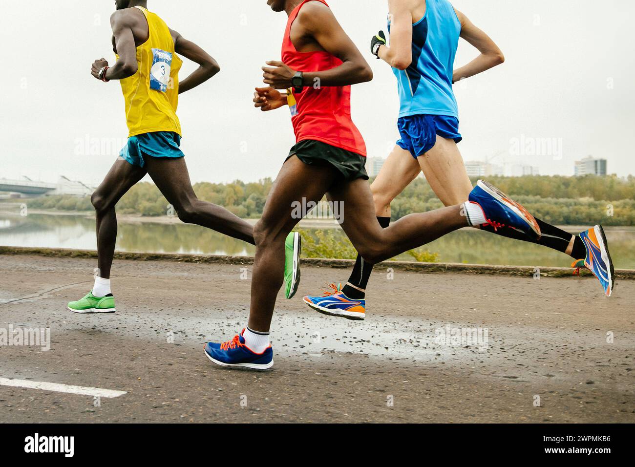 three runners dressed in bright sports clothes race along calm river ...