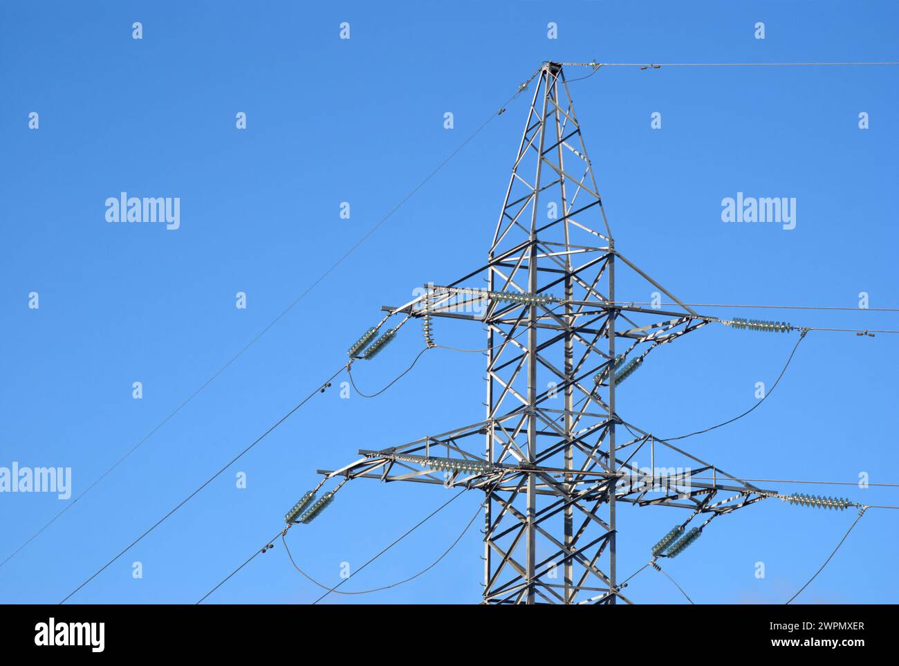 Top section of high-voltage power line metal prop on clear blue sky as ...