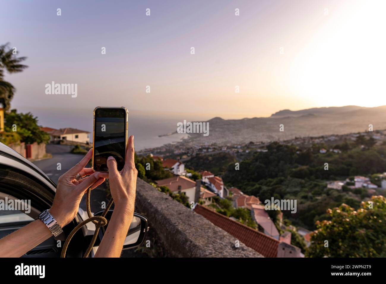 Woman taking a cell phone photo over the rooftops of Funchal, Madeira ...