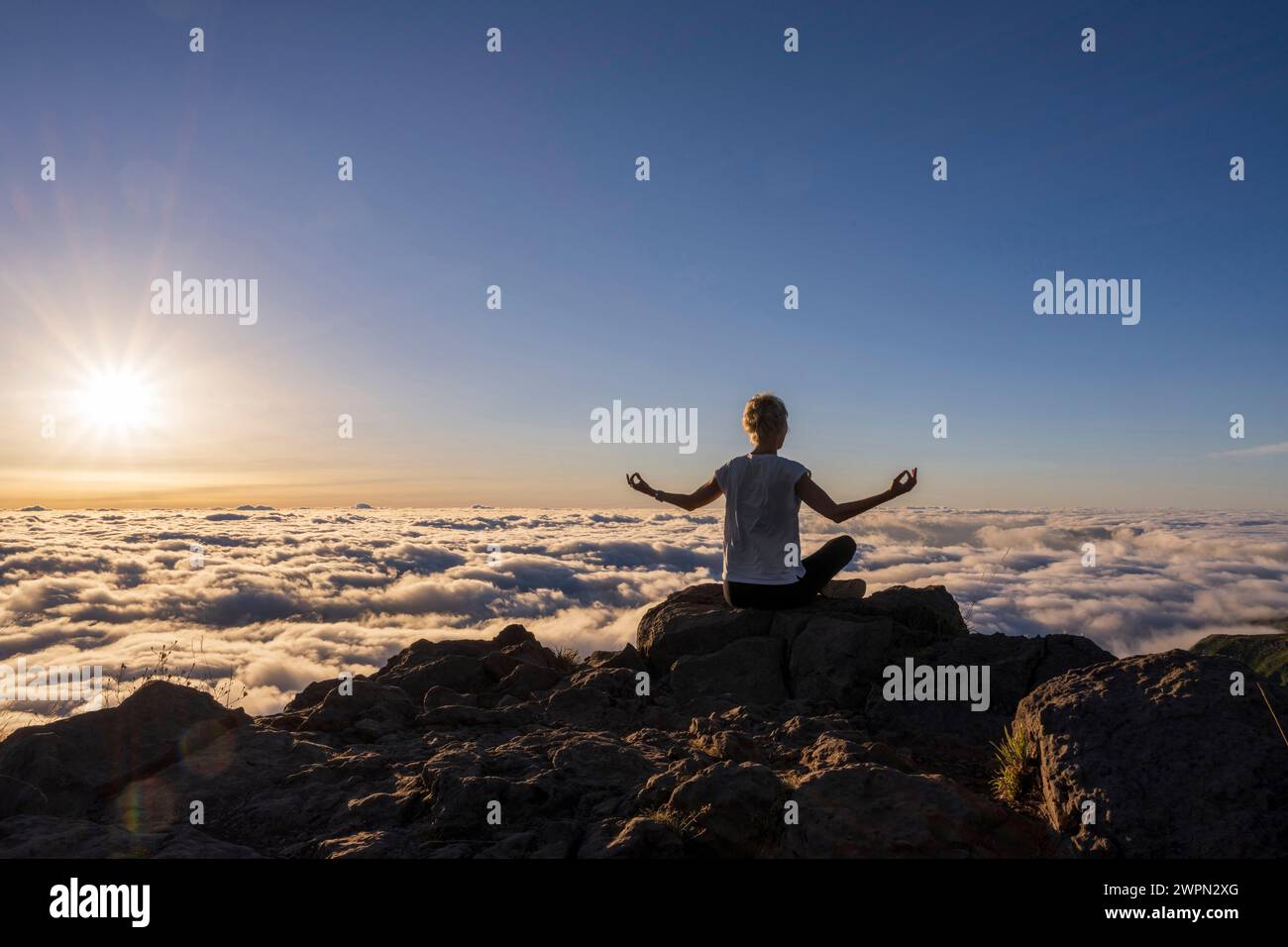Woman doing yoga and relaxation exercises at sunrise above the clouds ...