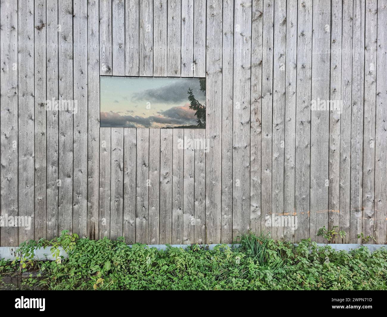 Evening sky with clouds reflected in the window of a rural wooden barn ...
