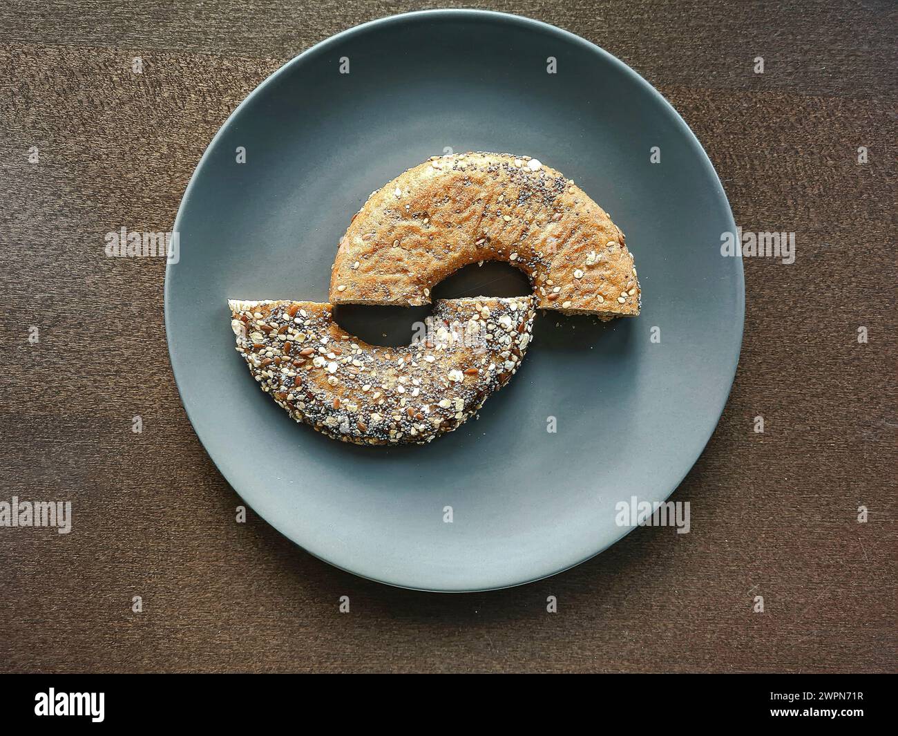 A bagel is cut in half on the bottom and the top with seeds on a gray ...