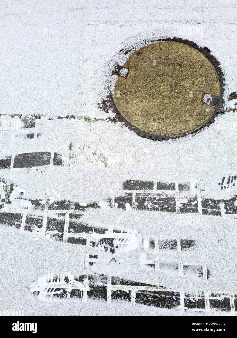 Tracks and patterns in the snow and the manhole cover covered in snow ...